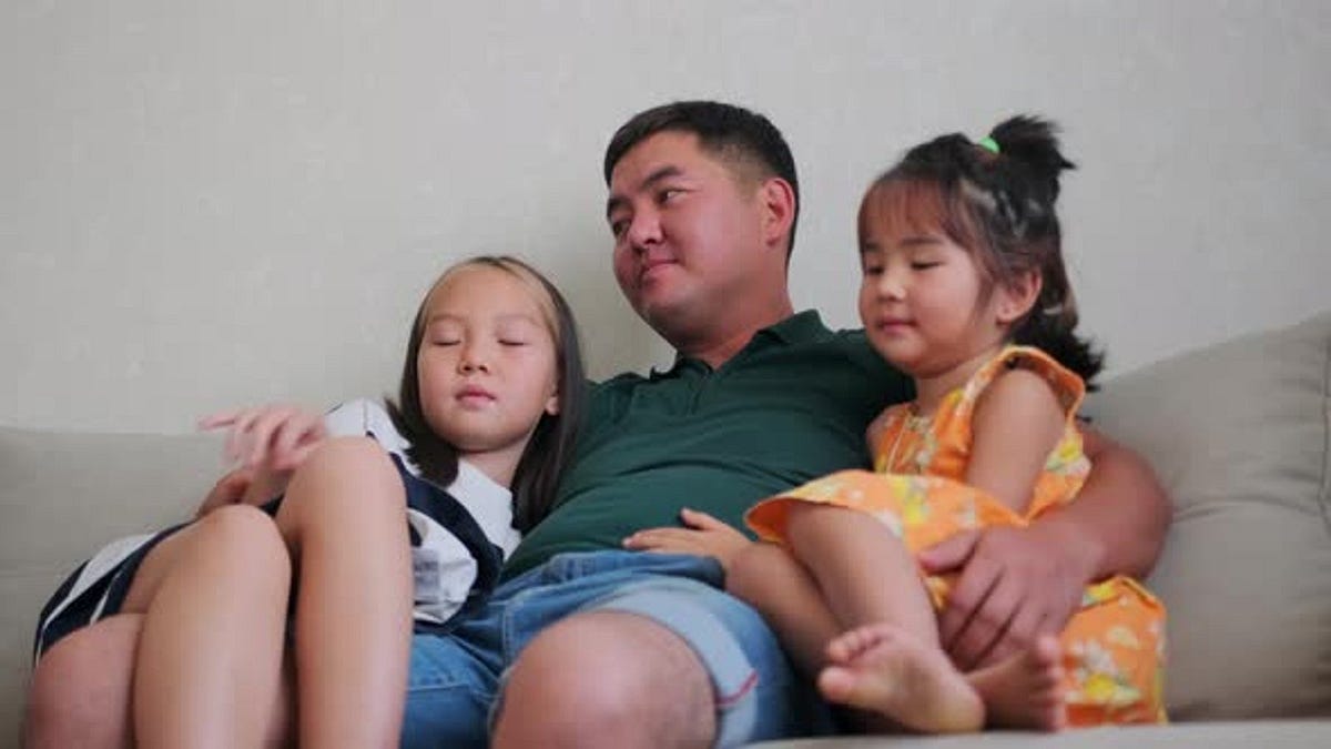 Loving father with two daughters hugging cutely sitting on sofa smiling ...