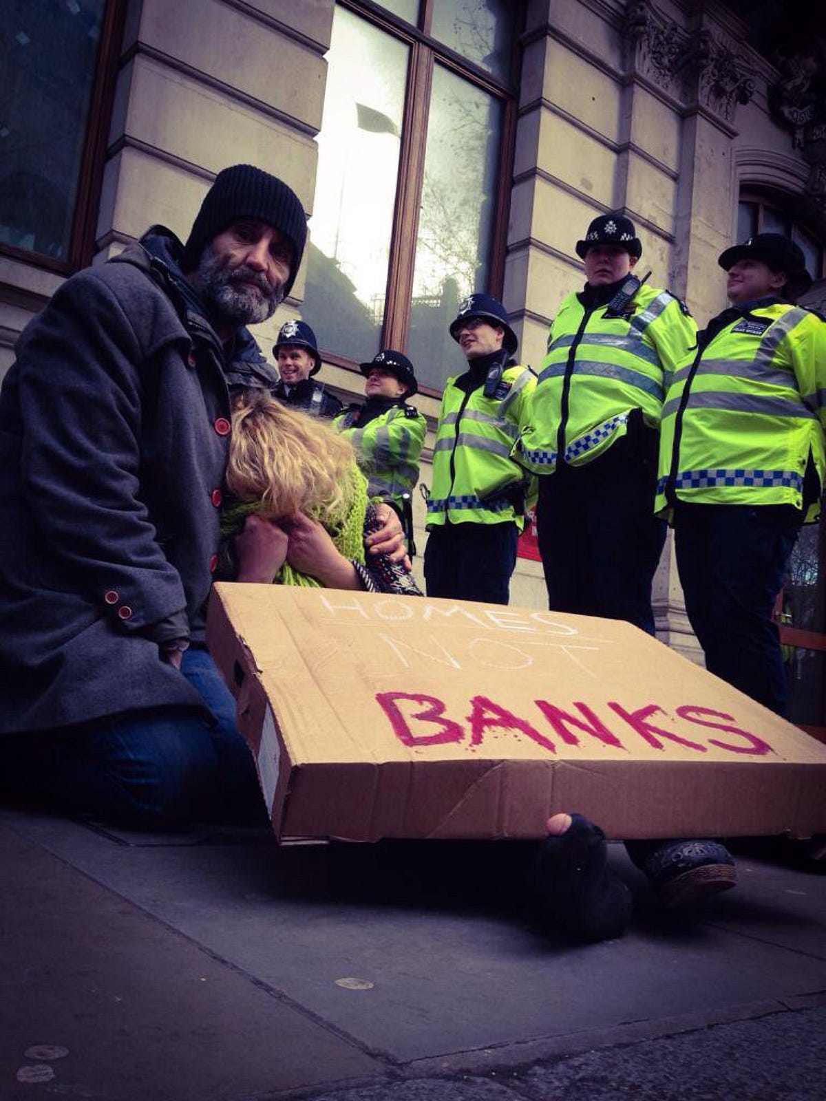 Homes not banks the makeshift placard says, the two homeless people sit ...